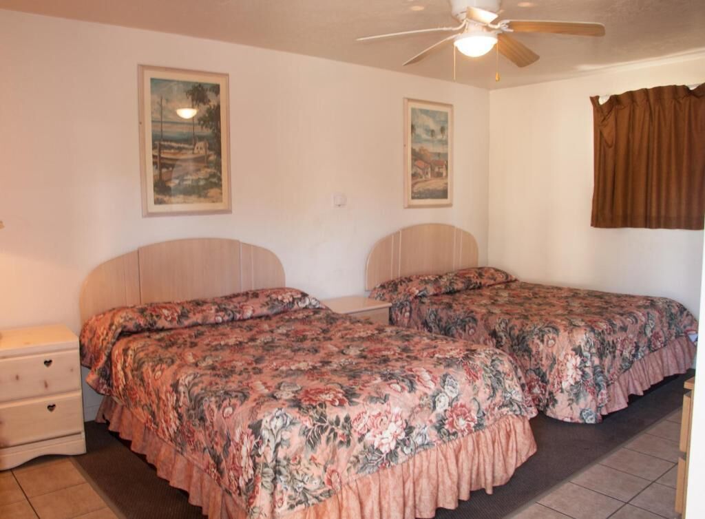 Quarto com duas camas, um ventilador de teto e duas pinturas nas paredes.