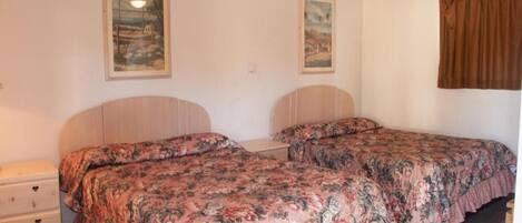 Quarto com duas camas, um ventilador de teto e duas pinturas nas paredes.