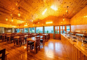 Interior em madeira com mesas, cadeiras, janelas amplas e uma área de buffet.