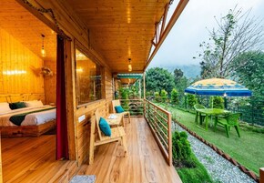 Uma cabana de madeira com varanda, uma cama e uma mesa com cadeiras.