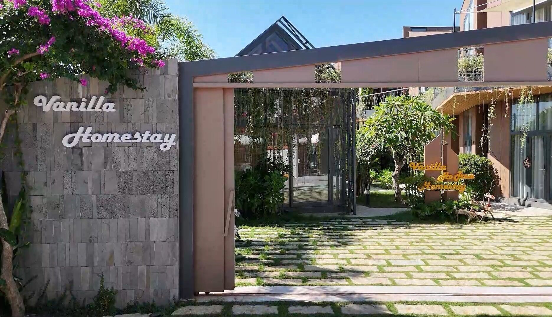 Uma entrada com portão para um imóvel chamado 'Vanilla Homestay', com um caminho pavimentado que leva ao edifício principal.