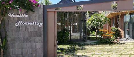 Uma entrada com portão para um imóvel chamado 'Vanilla Homestay', com um caminho pavimentado que leva ao edifício principal.