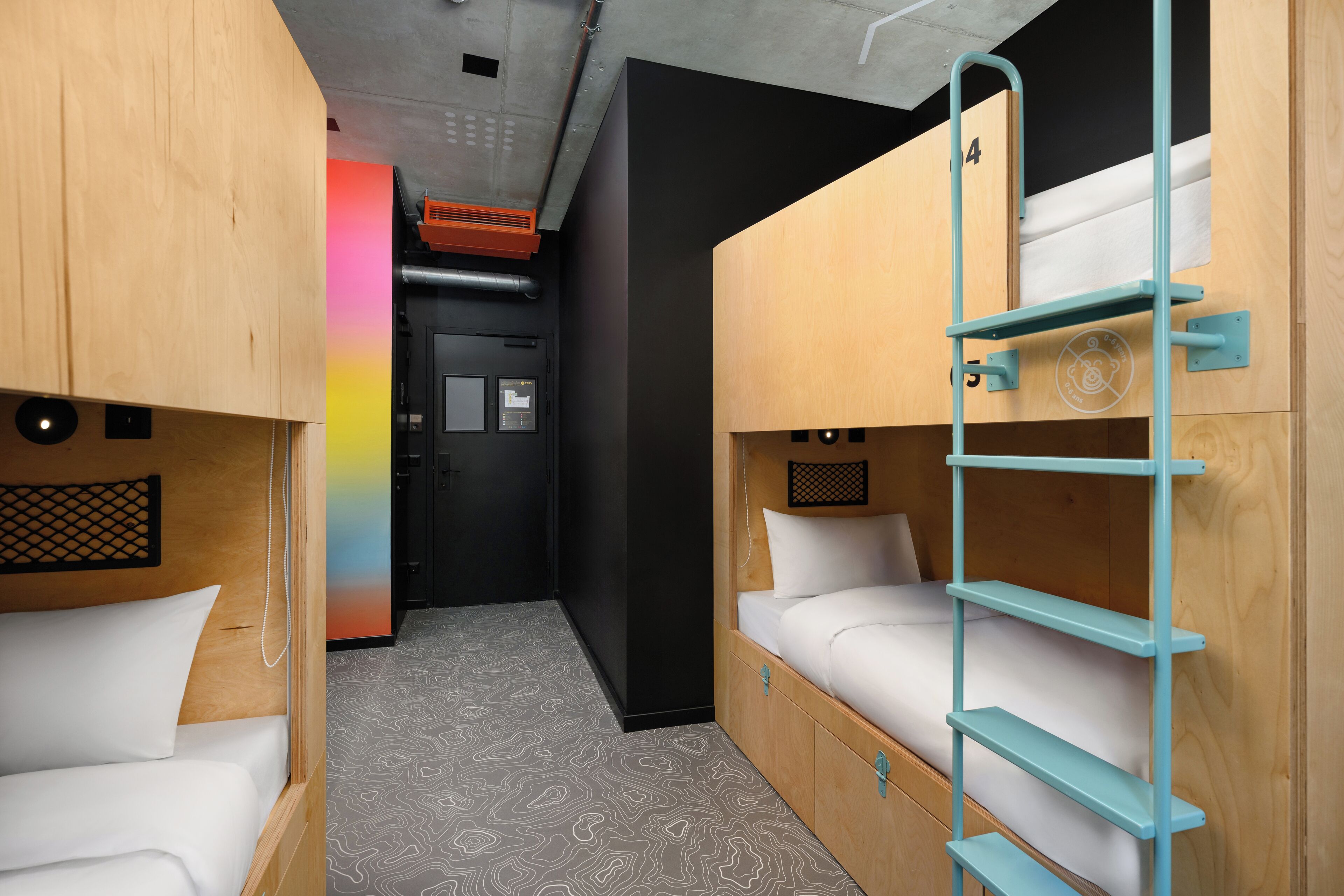 Quarto compacto e moderno com beliches, uma escada e uma pequena mesa.
