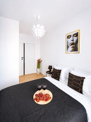 Quarto com cama, mesa de cabeceira, abajur, vaso com flores e quadro na parede.
