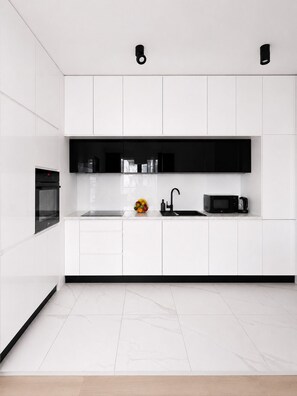 Cozinha moderna com armários brancos, bancada preta, pia, micro-ondas e fogão.
