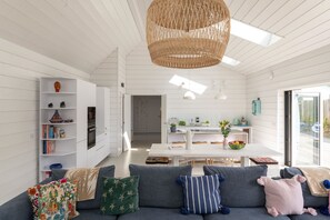 Uma sala de estar moderna com um sofá cinzento, uma estante e uma área de refeições com mesa e cadeiras.