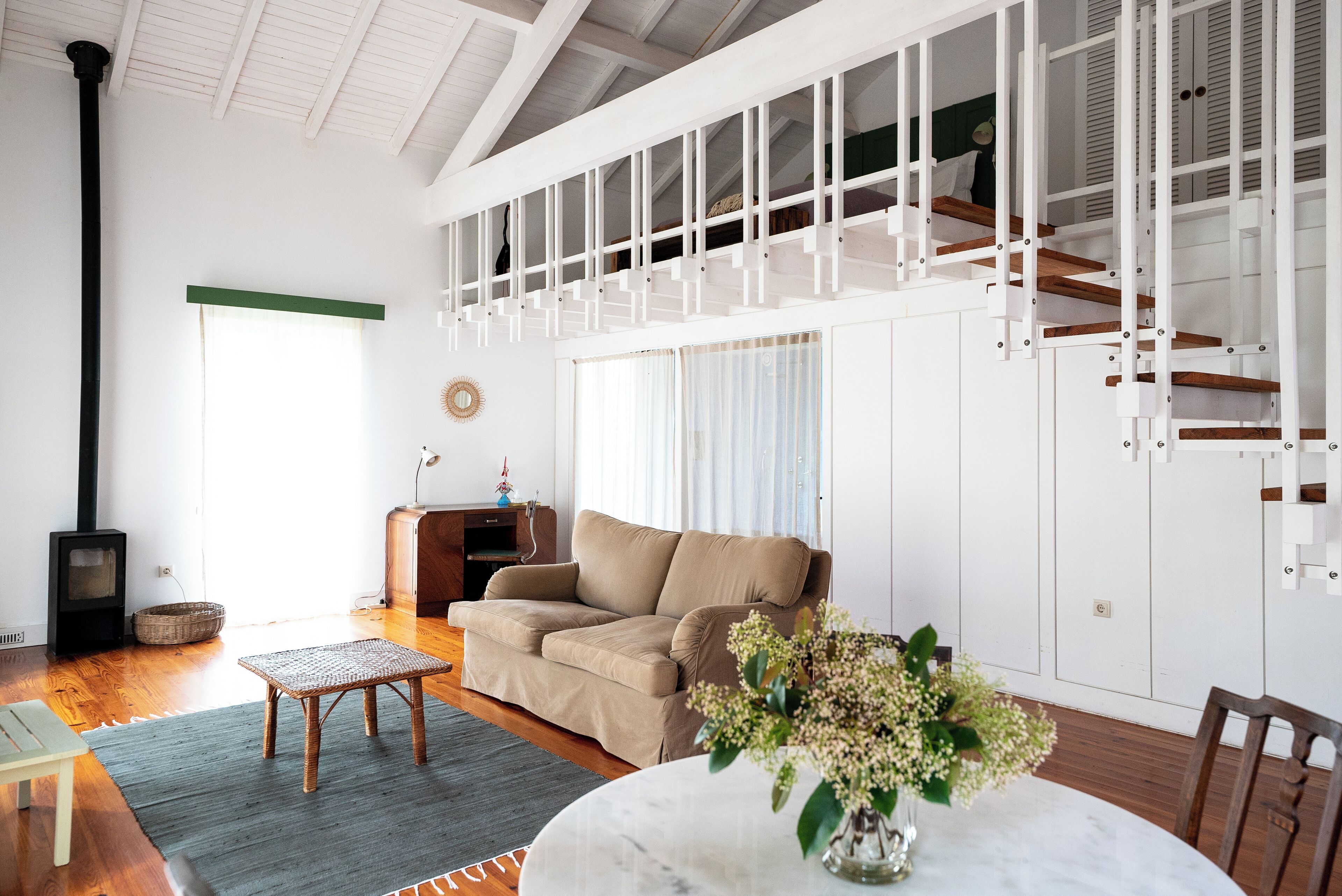 Uma sala de estar espaçosa com teto alto, escada embutida, sofá, mesa de centro e lareira.