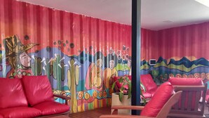 Um quarto com um mural vibrante, mobiliário estofado em vermelho e piso de madeira.
