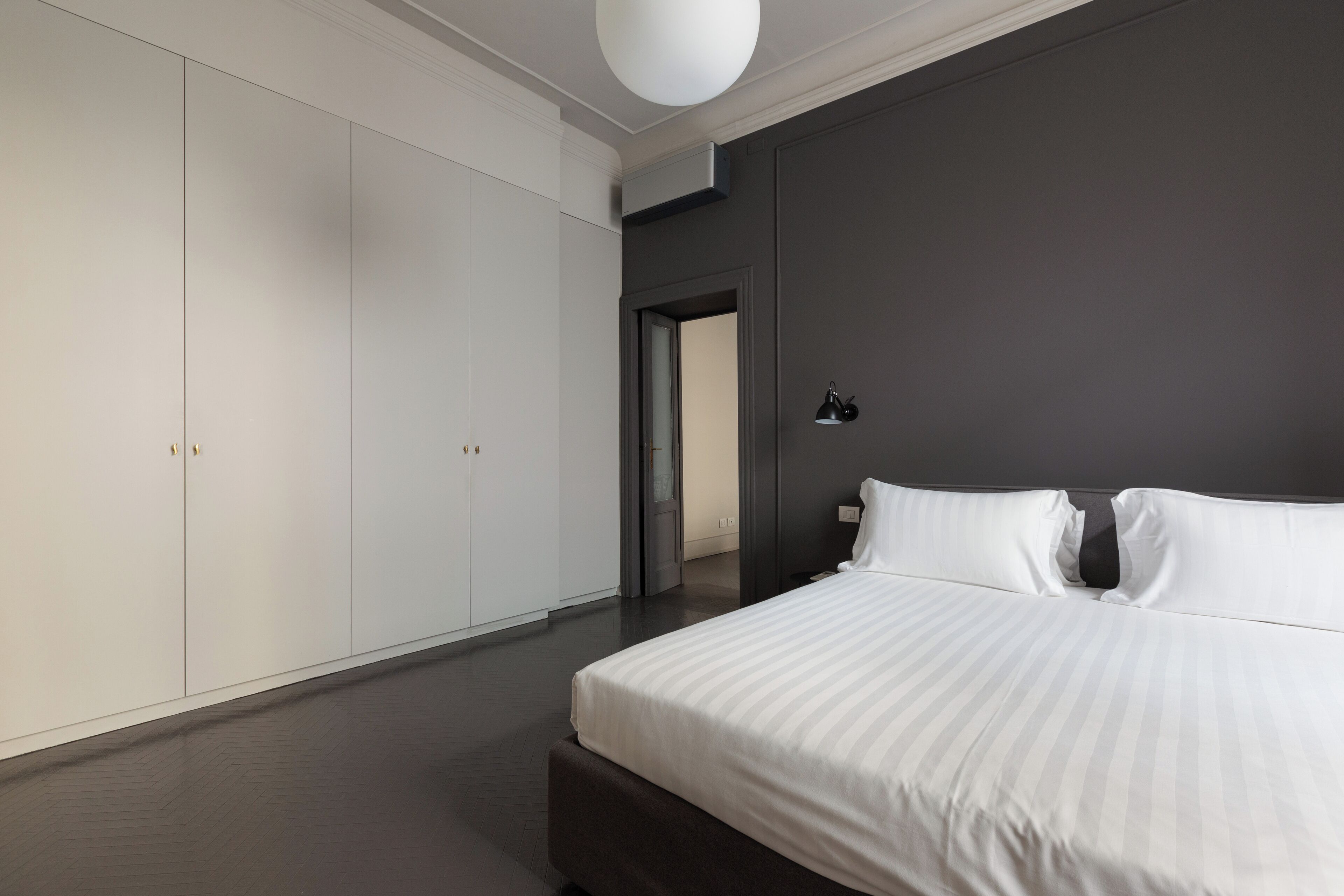 Quarto moderno com uma cama grande, um guarda-roupa e uma porta que dá para outro espaço.