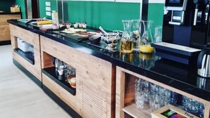Uma área de buffet com diversas opções de comida, uma máquina de café e um canto para chá.