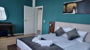 Cama bem arrumada com roupa de cama branca e cinza, cabeceira de madeira e um quadro na parede.