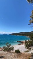 Paisagem costeira com mar azul límpido, costa rochosa e vegetação escassa.
