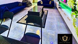 Uma sala de estar moderna com um sofá azul, cadeiras pretas, uma mesa de centro de vidro e uma TV na parede.
