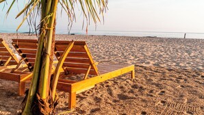 Uma praia com espreguiçadeiras de madeira e uma palmeira.
