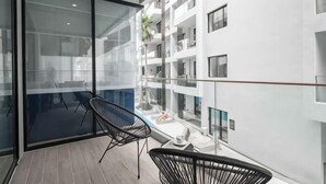 Um apartamento moderno com varanda de vidro, cadeiras de vime preto e vista para o interior do edifício.