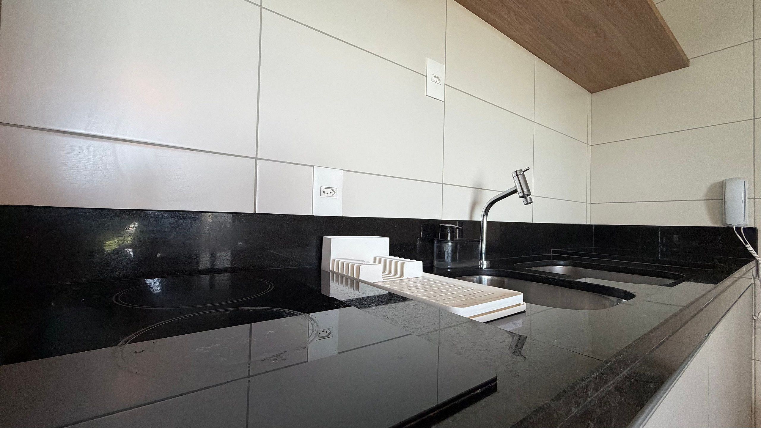 Cozinha moderna com bancadas pretas, pia de aço inoxidável e dosador de sabão branco.