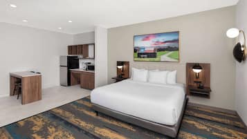 Quarto de hotel moderno com uma cama grande, uma mesa, uma cozinha compacta e um quadro na parede.