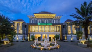Um hotel com fachada moderna, entrada central e área de jardim bem iluminada com estátuas decorativas.