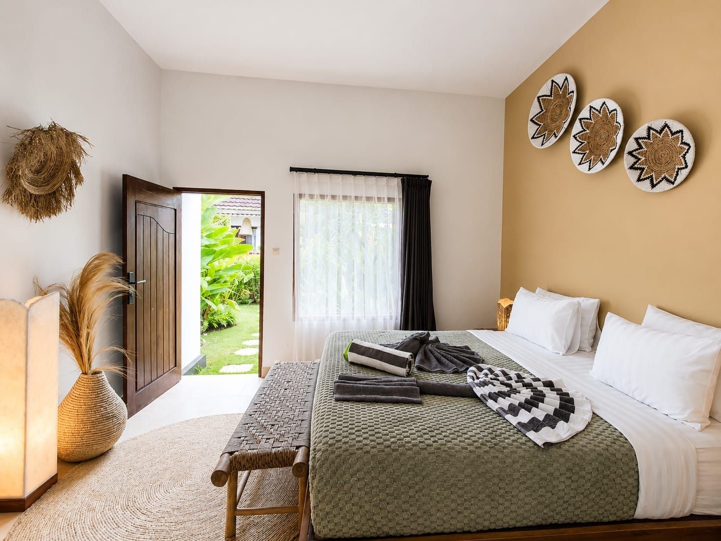 Quarto de hotel com cama, mesa de cabeceira, janela com cortinas, porta para um jardim e arte nas paredes.