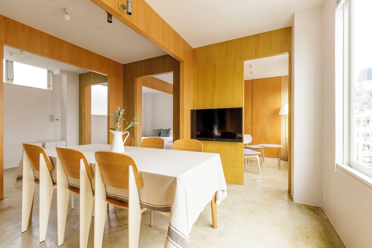 Uma área de refeições moderna com uma mesa grande, cadeiras de madeira, uma televisão de tela plana e vista para a cidade através de grandes janelas.