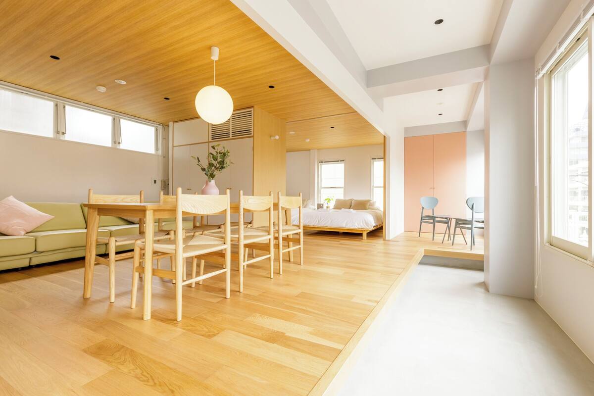 Um espaço de estar moderno e aberto, com uma mesa de jantar de madeira e cadeiras, um sofá verde e uma janela grande que traz luz natural.