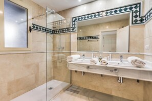 Uma casa de banho moderna com chuveiro envidraçado, um espelho grande e uma toucador com várias pias e suportes para toalhas.