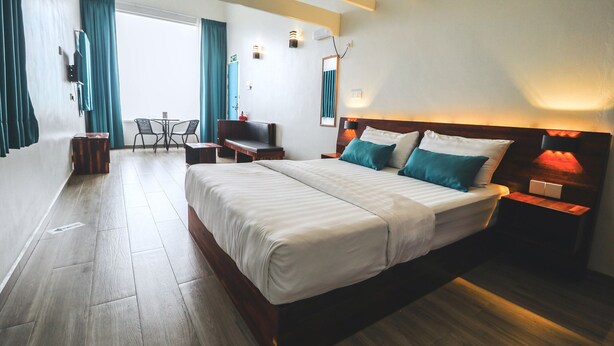 Quarto de hotel com uma cama grande, uma mesa de trabalho e uma cadeira. Vê-se a paisagem exterior pela janela.
