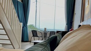Quarto com uma cama, escada, janela com cortinas e uma pequena mesa com cadeiras.