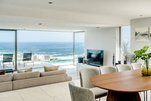 Uma sala de estar moderna com uma televisão grande, assentos confortáveis e vista para o oceano.