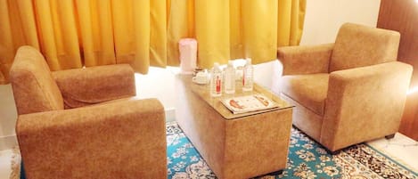 Um quarto com duas poltronas bege, uma mesa de centro de vidro e um tapete estampado.