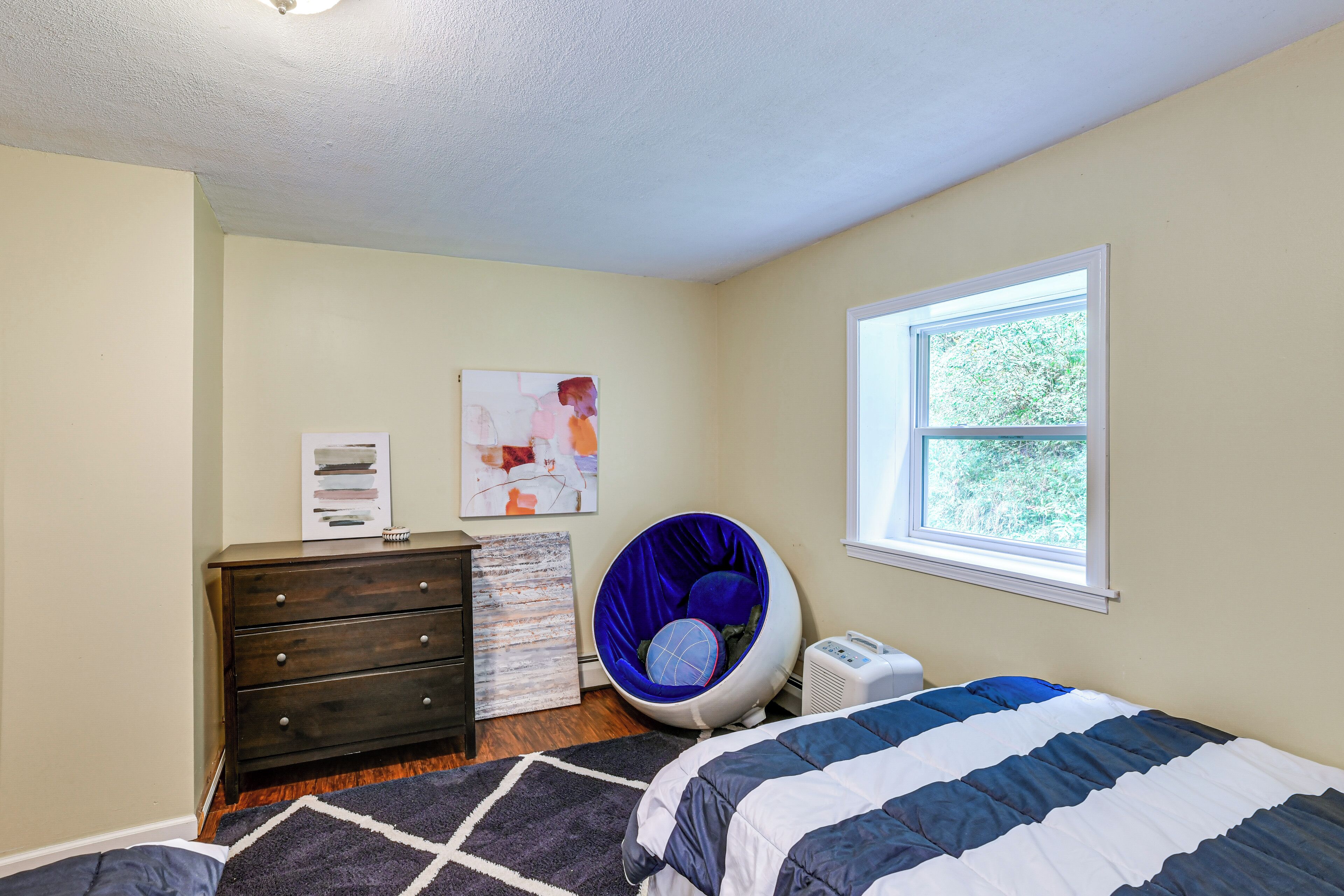Quarto com cama, cômoda, cadeira e obra de arte na parede.