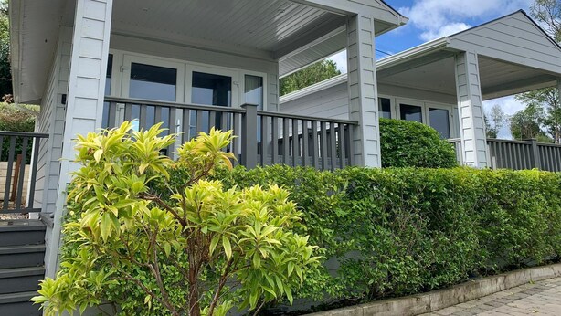 Uma casa de dois andares com varanda coberta e um hedge bem cuidado.