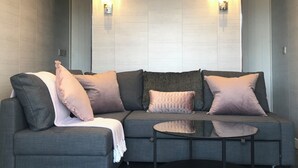 Uma sala de estar moderna com um sofá modular cinza, duas mesas laterais e um grande candeeiro fixado na parede.