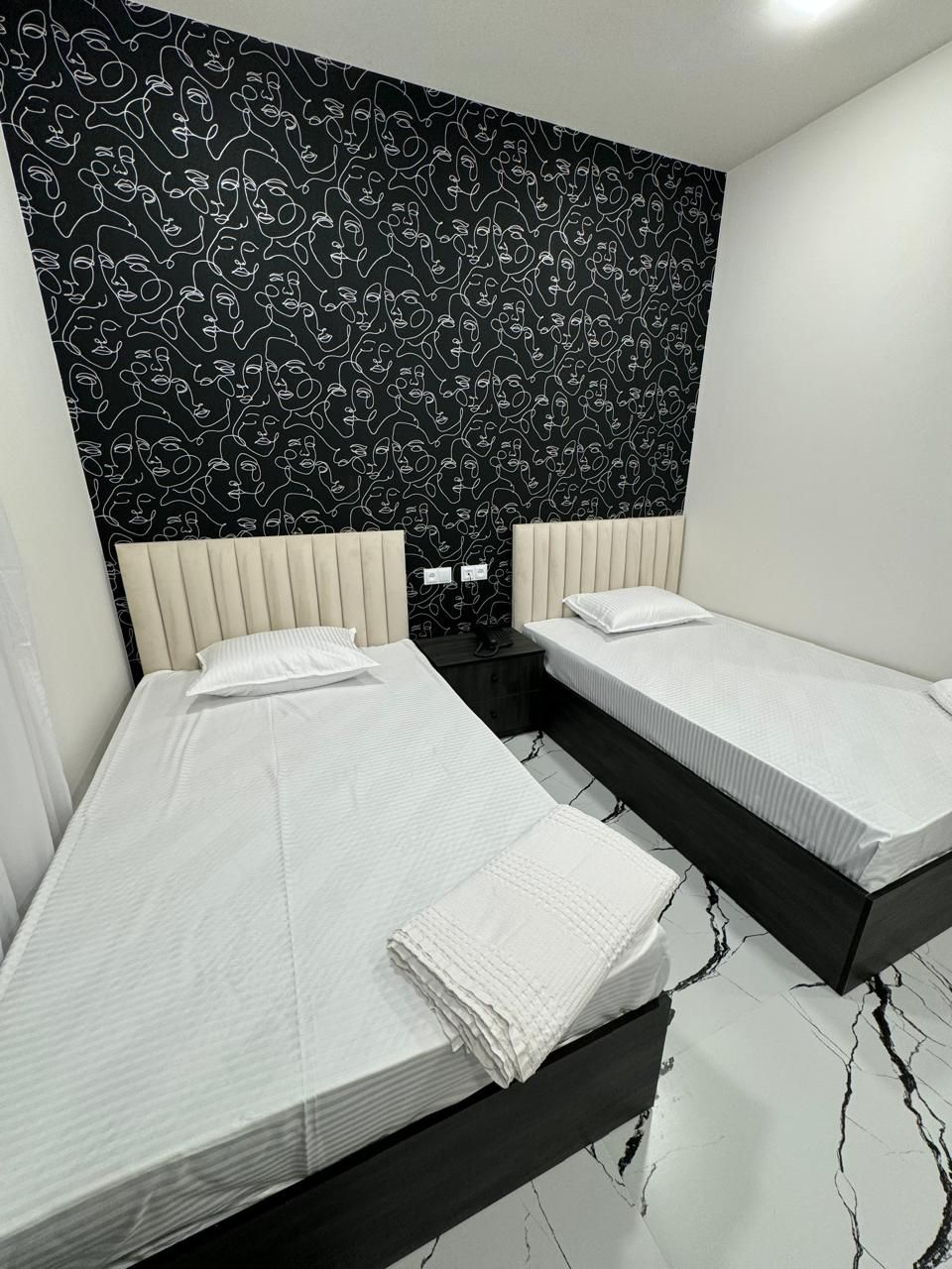 Quarto moderno com duas camas, parede estampada em preto e branco e piso de mármore.
