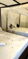 Uma cama com mosquiteiro, roupa de cama branca com desenhos de estrelas e uma mesa de cabeceira com um livro.