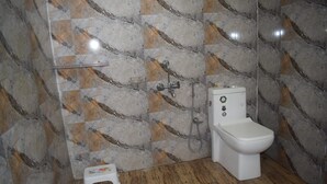 Casa de banho com sanita, chuveiro e um banquinho pequeno.