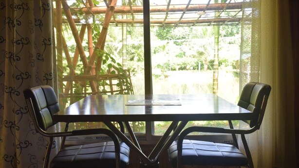 Uma mesa com quatro cadeiras, uma janela com vista para vegetação e uma estrutura de bambu do lado de fora.