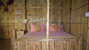 Quarto decorado com motivos de bambu, com uma cama, almofadas e uma pequena mesa de cabeceira de madeira.