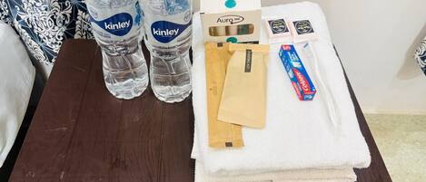Uma mesa de madeira com duas garrafas de água Kinley, uma toalha branca, uma caixa de Auro 360 e um pacote de lenços de papel.