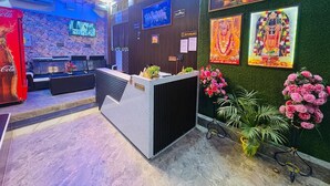 Uma área de recepção com design moderno, incluindo balcão de atendimento, espaço para sentar e elementos decorativos como quadros e plantas.