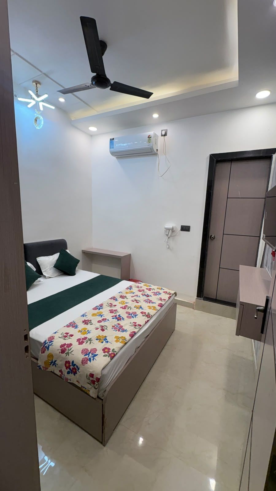 Quarto com cama, mesa de cabeceira, guarda-roupa, ventoinha no teto e ar condicionado.