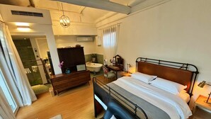Quarto de hotel com cama, escrivaninha, cadeira, banheiro e televisão.