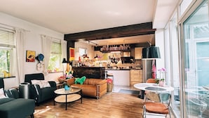 Uma sala de estar moderna com sofá, mesa de centro e cadeiras, uma cozinha com armários de madeira e uma área de jantar com mesa e cadeiras.