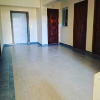 Um corredor amplo com piso ladrilhado, duas portas de madeira e uma pequena janela.