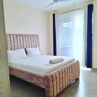 Uma cama bem arrumada com cabeceira, uma janela com cortinas e um ventilador de teto.
