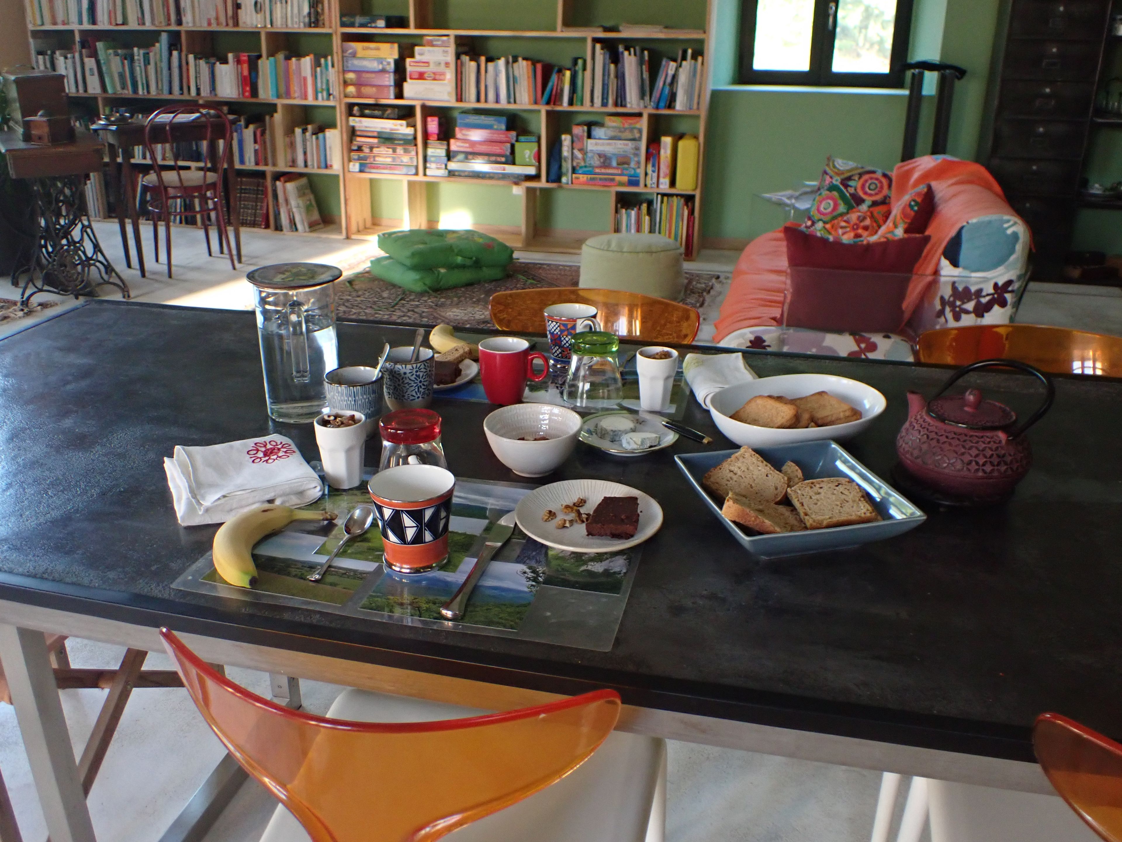 Mesa de jantar com diversos pratos, um bule e uma estante de livros ao fundo.