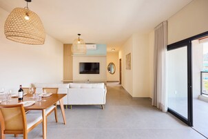Uma sala de estar moderna com área de jantar, sofá, televisão montada na parede e uma grande janela com cortinas.