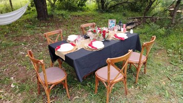 Mesa de jantar ao ar livre posta com pratos brancos, guardanapos vermelhos e toalha de mesa preta, cercada por cadeiras de madeira.