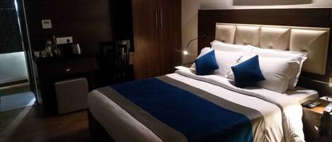 Quarto de hotel com cama, mesa de cabeceira, luminária e um quadro na parede.