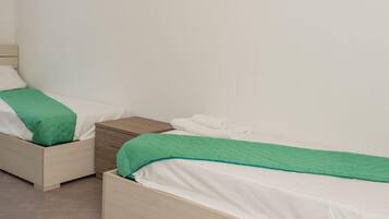 Duas camas de solteiro com roupa de cama verde, um criado-mudo de madeira e uma toalha branca sobre ele.